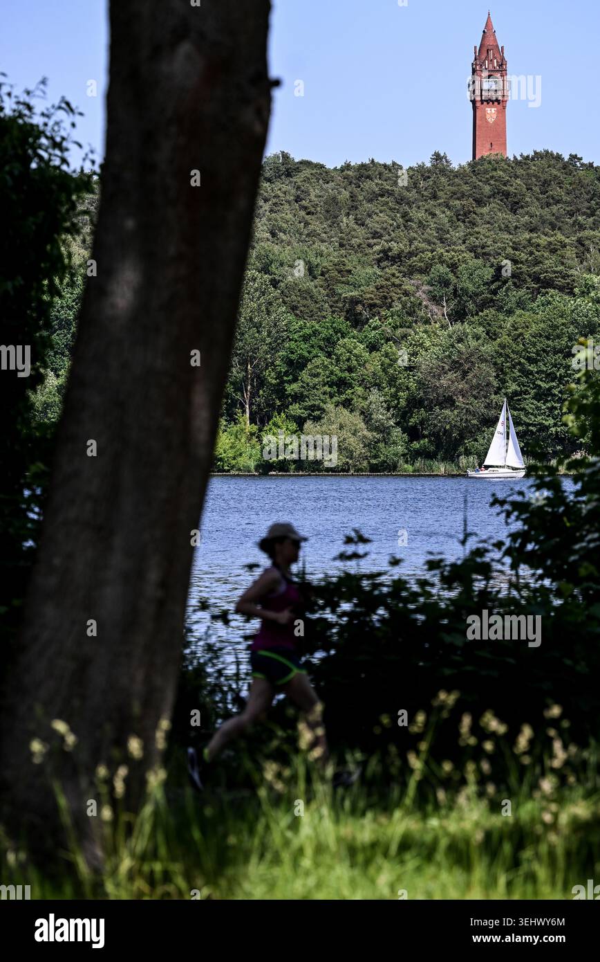 26 May 2026, Berlin: A woman jogs along the banks of the Havel in front ...