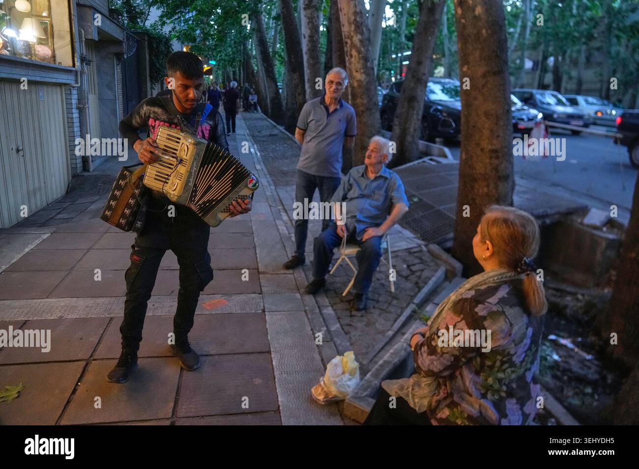 A street musician plays an accordion on a sidewalk in northern Tehran ...
