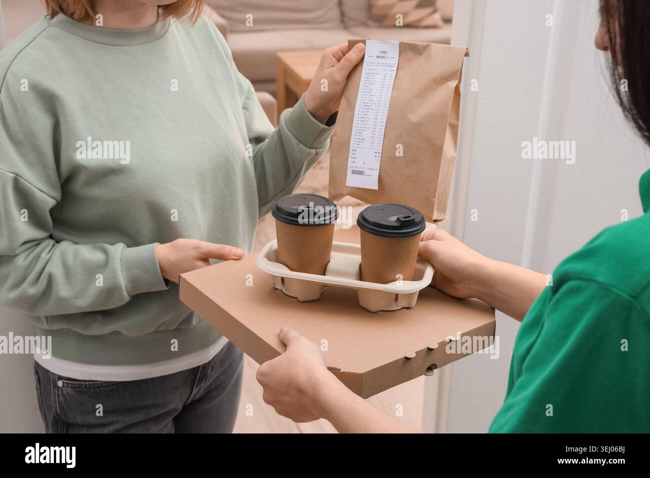 Young woman receiving food with coffee cups from courier at doorway ...