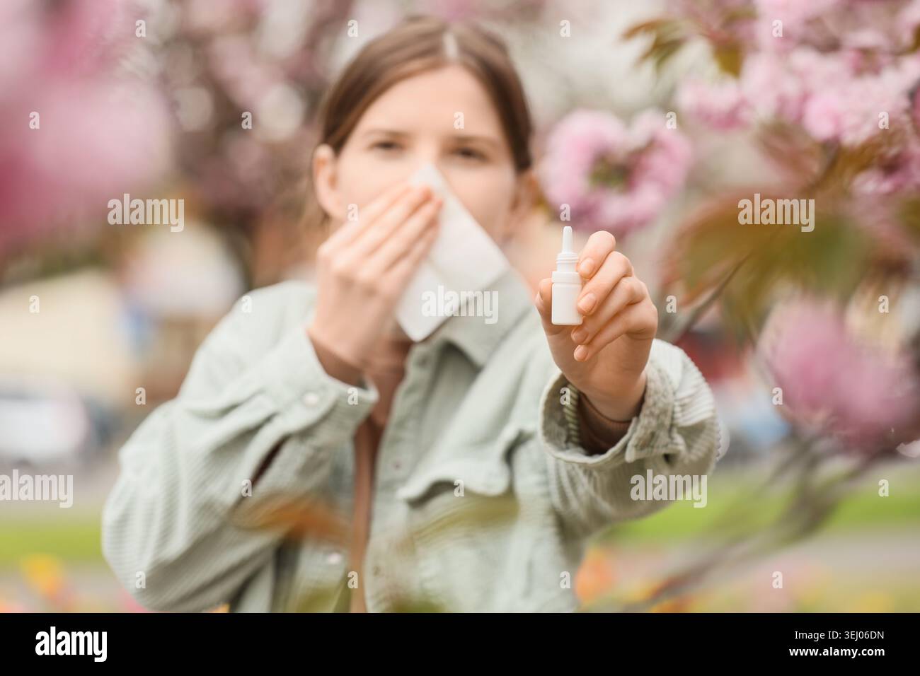 Allergic young woman with tissue and eye drops in park on spring day ...
