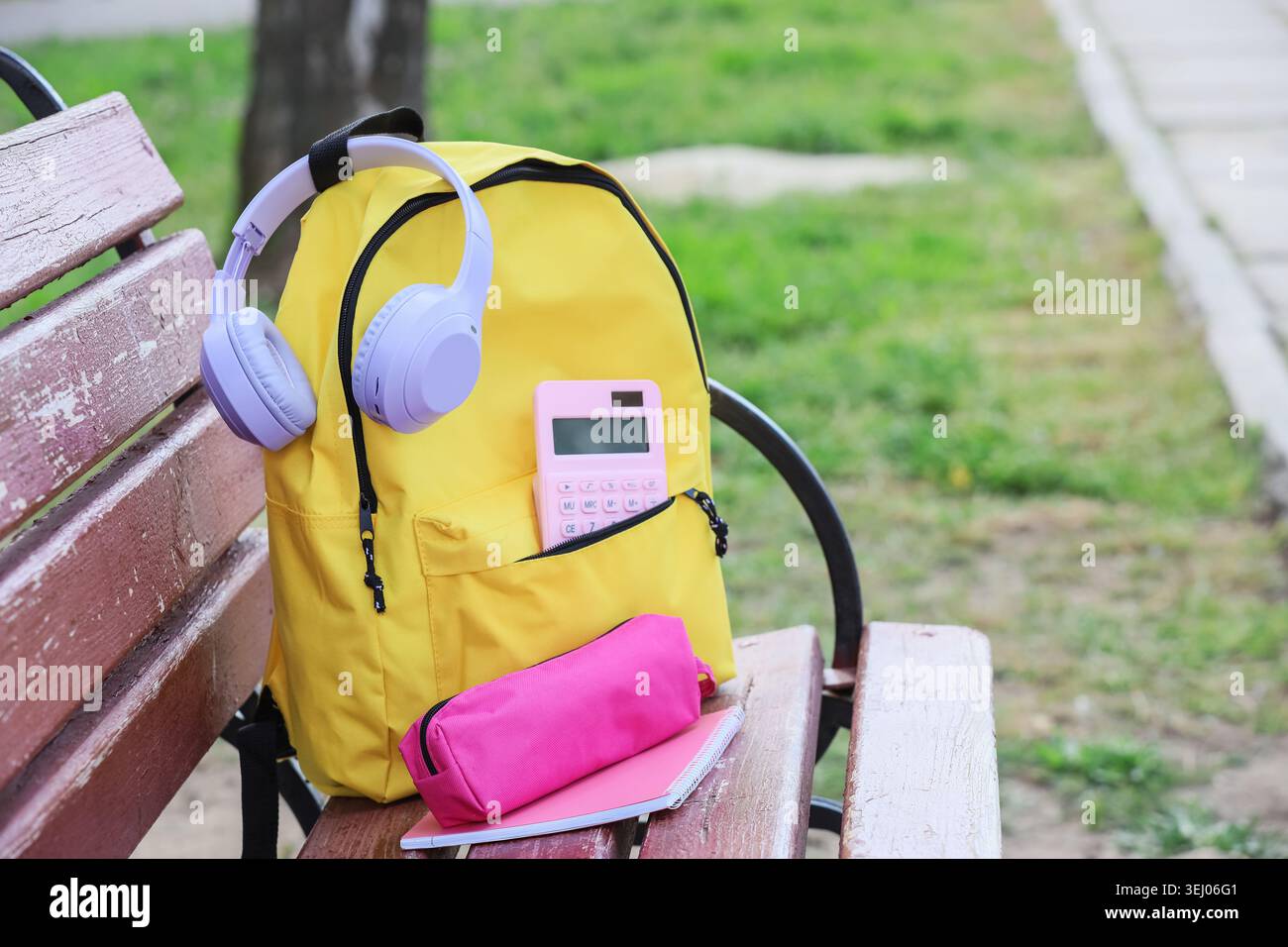 Yellow backpack with school stationery and headphones on bench in park ...