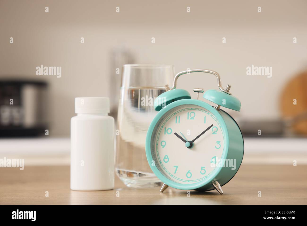 Alarm clock with pill bottle and glass of water on table in kitchen ...