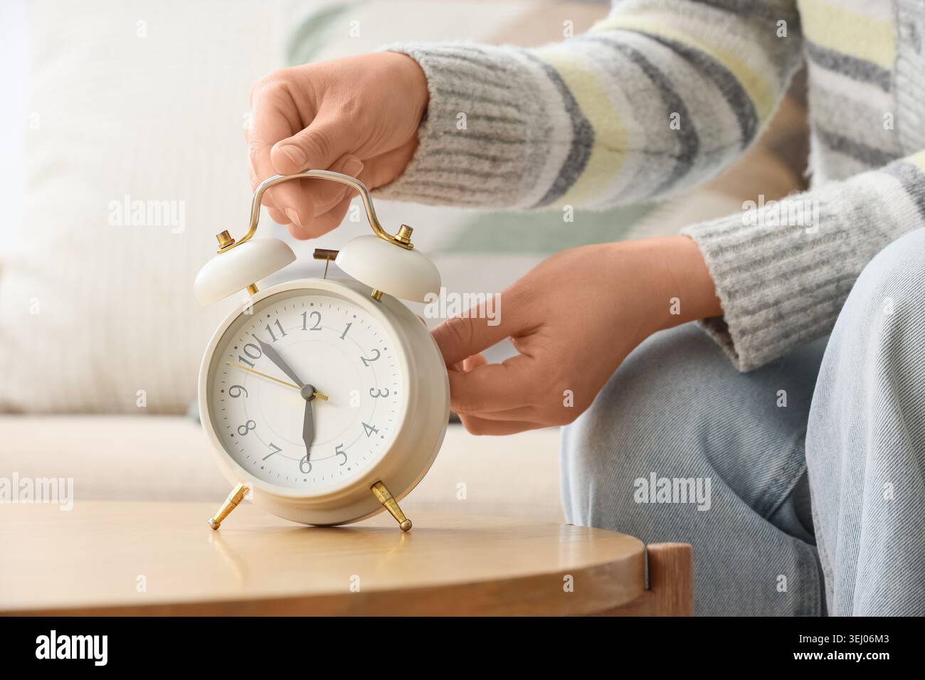 Woman changing alarm clock for daylight saving time on table at home ...