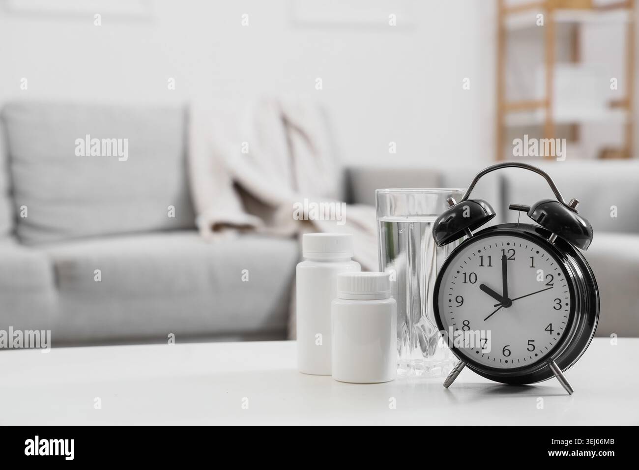 Alarm clock with pill bottles and glass of water on table in room Stock ...