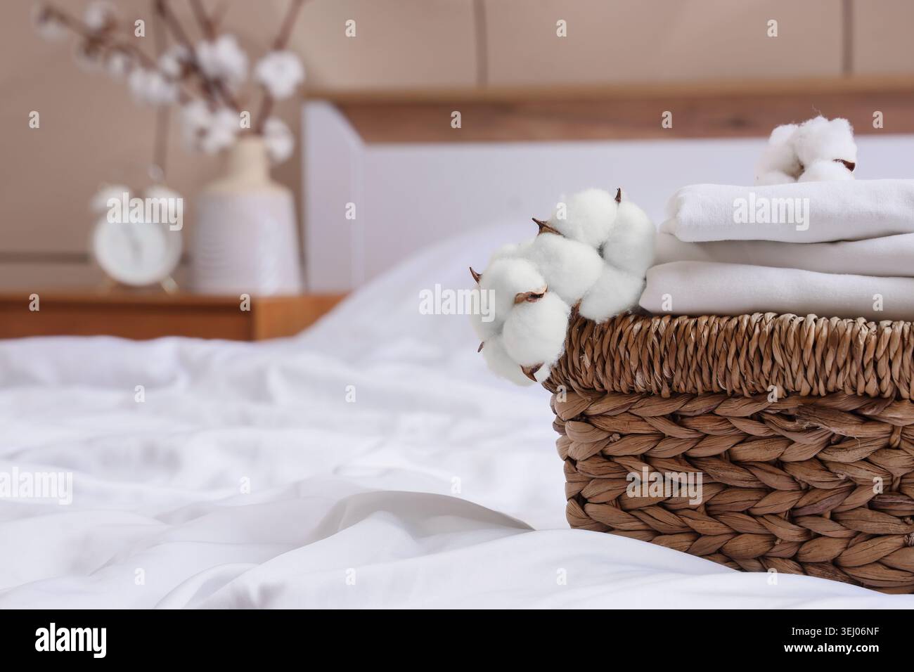 Wicker basket with cotton flowers and white linen in bedroom, closeup ...