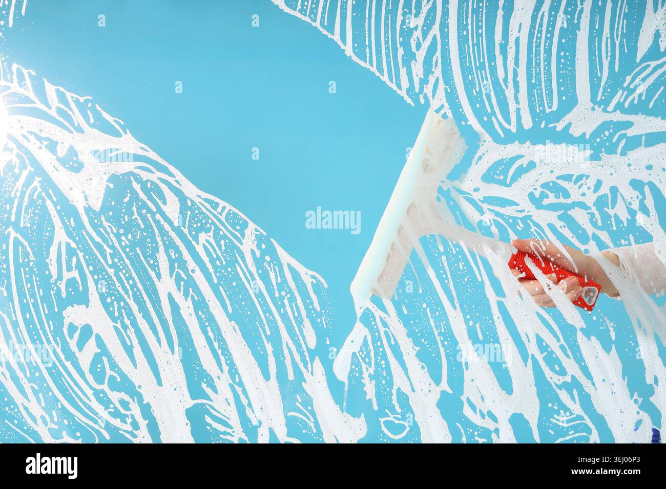 Female hand with squeegee and detergent washing glass against blue ...