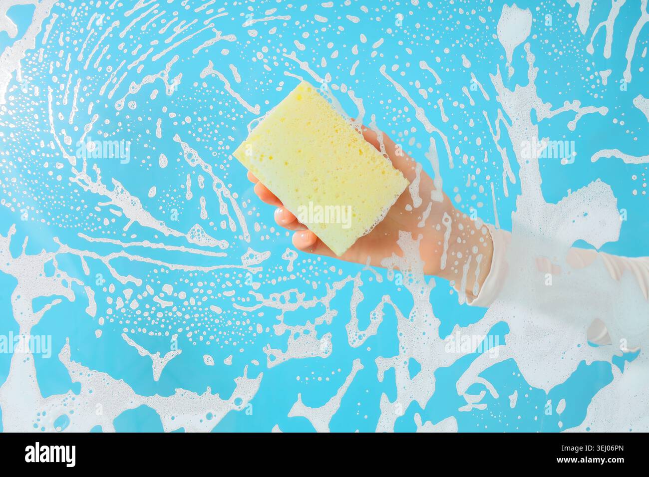Female hand with sponge and detergent washing glass against blue ...