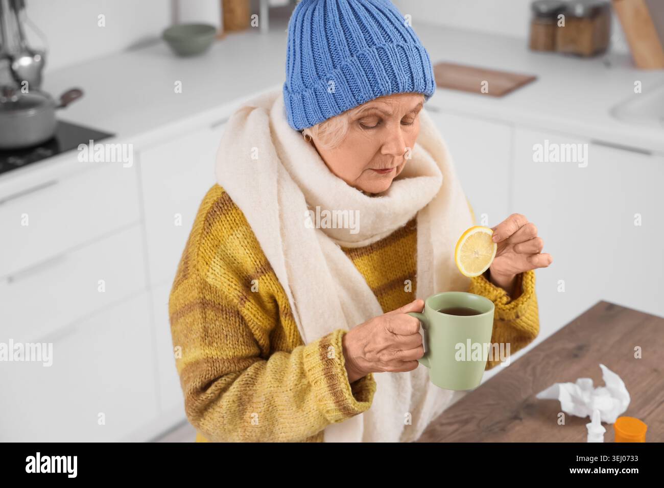 Sick elderly woman putting lemon into cup of tea in kitchen Stock Photo ...