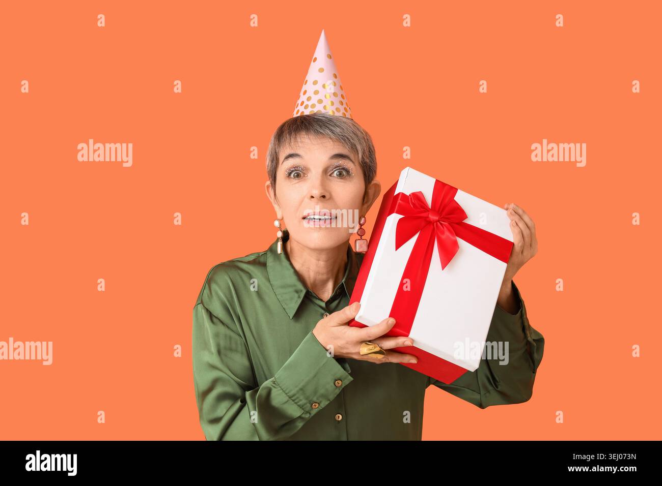 Mature woman in party hat with Birthday gift on orange background Stock ...