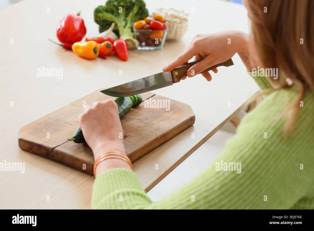 Mature woman cutting cucumber at table in kitchen, closeup Stock Photo ...