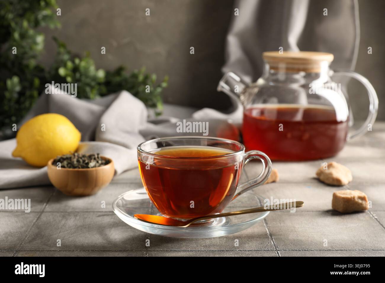 Composition with cup of black tea, teapot and dry leaves on grey tile ...