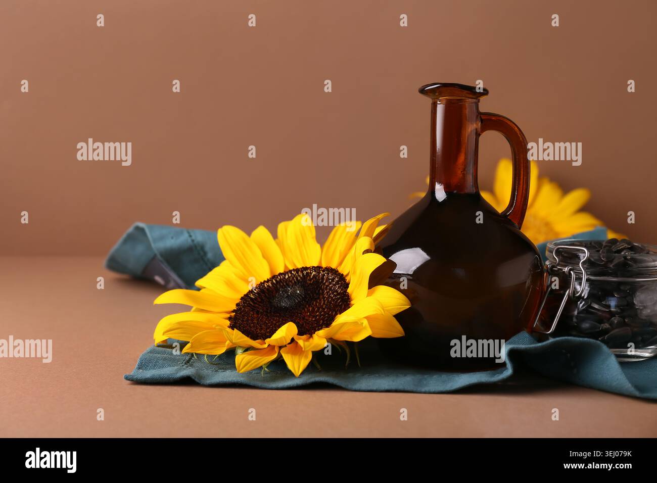 Jug of oil, sunflower and jar with seeds on brown background Stock ...