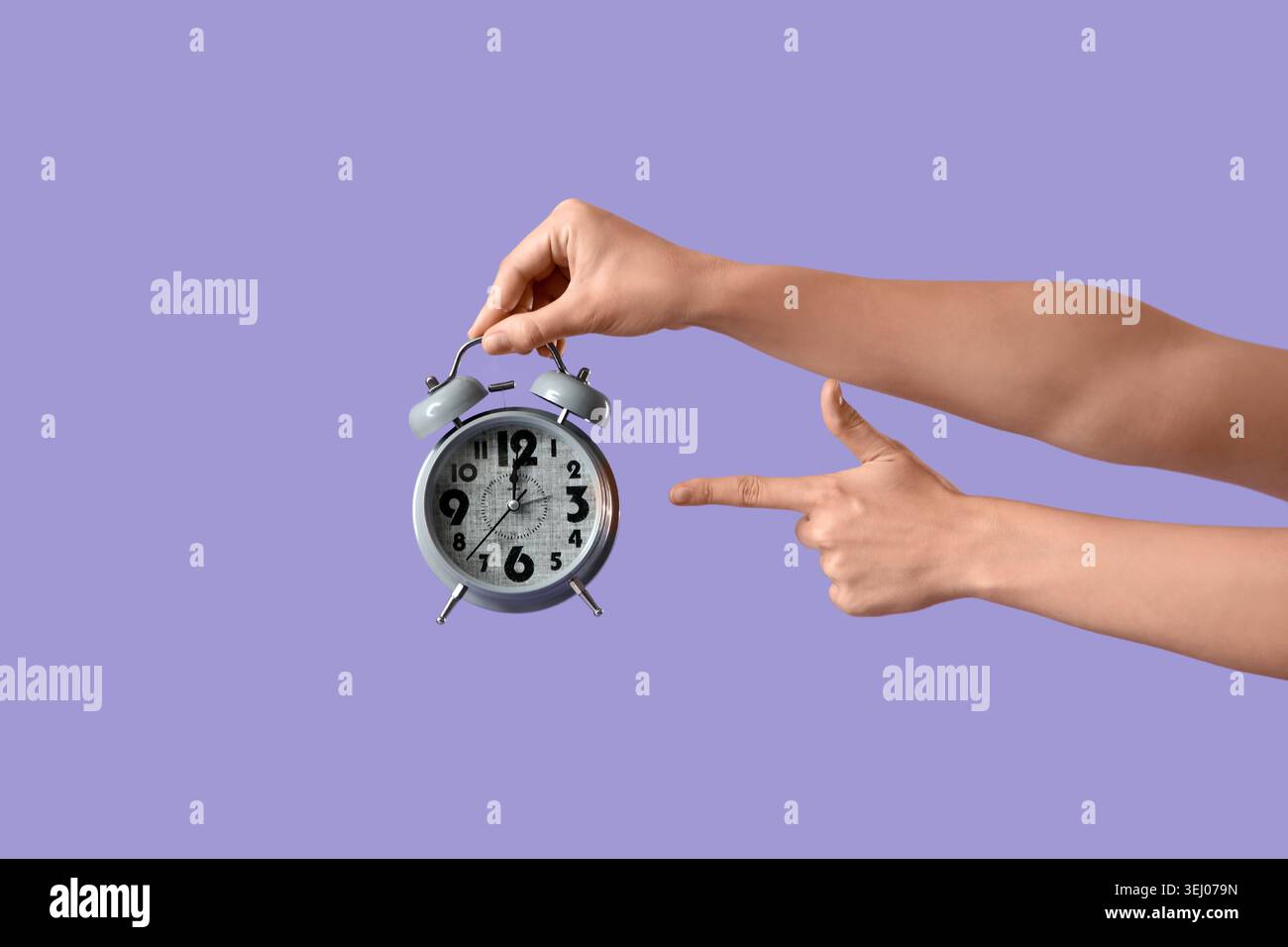 Female hands pointing at alarm clock on lilac background Stock Photo ...