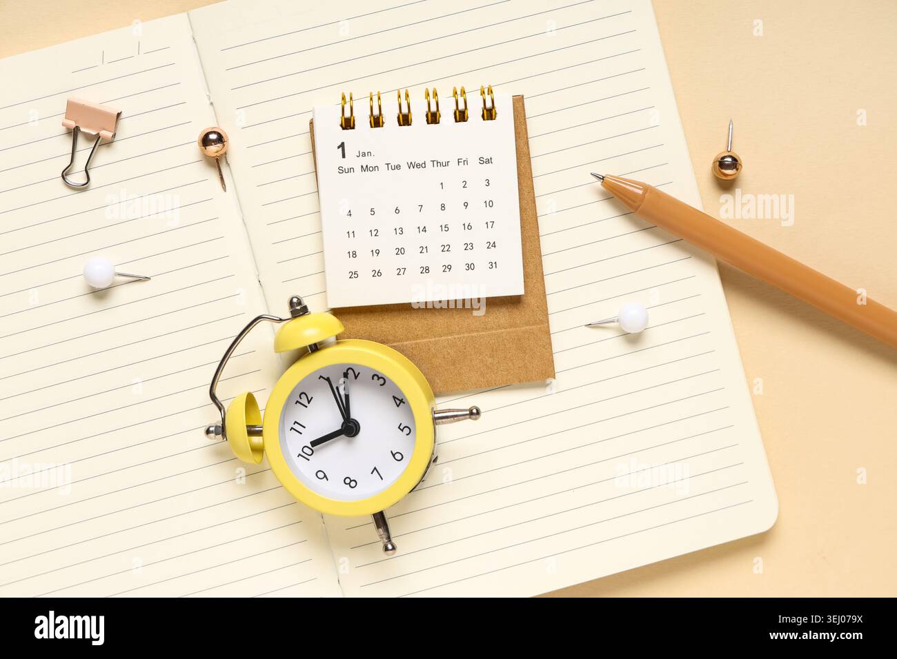 Calendar with alarm clock, notebook, paper pins and pen on beige ...