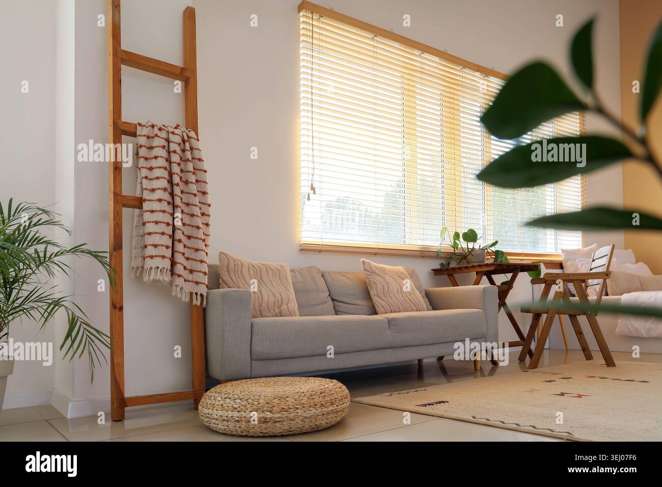 Interior of living room with grey sofa, table, pouf and stepladder near ...
