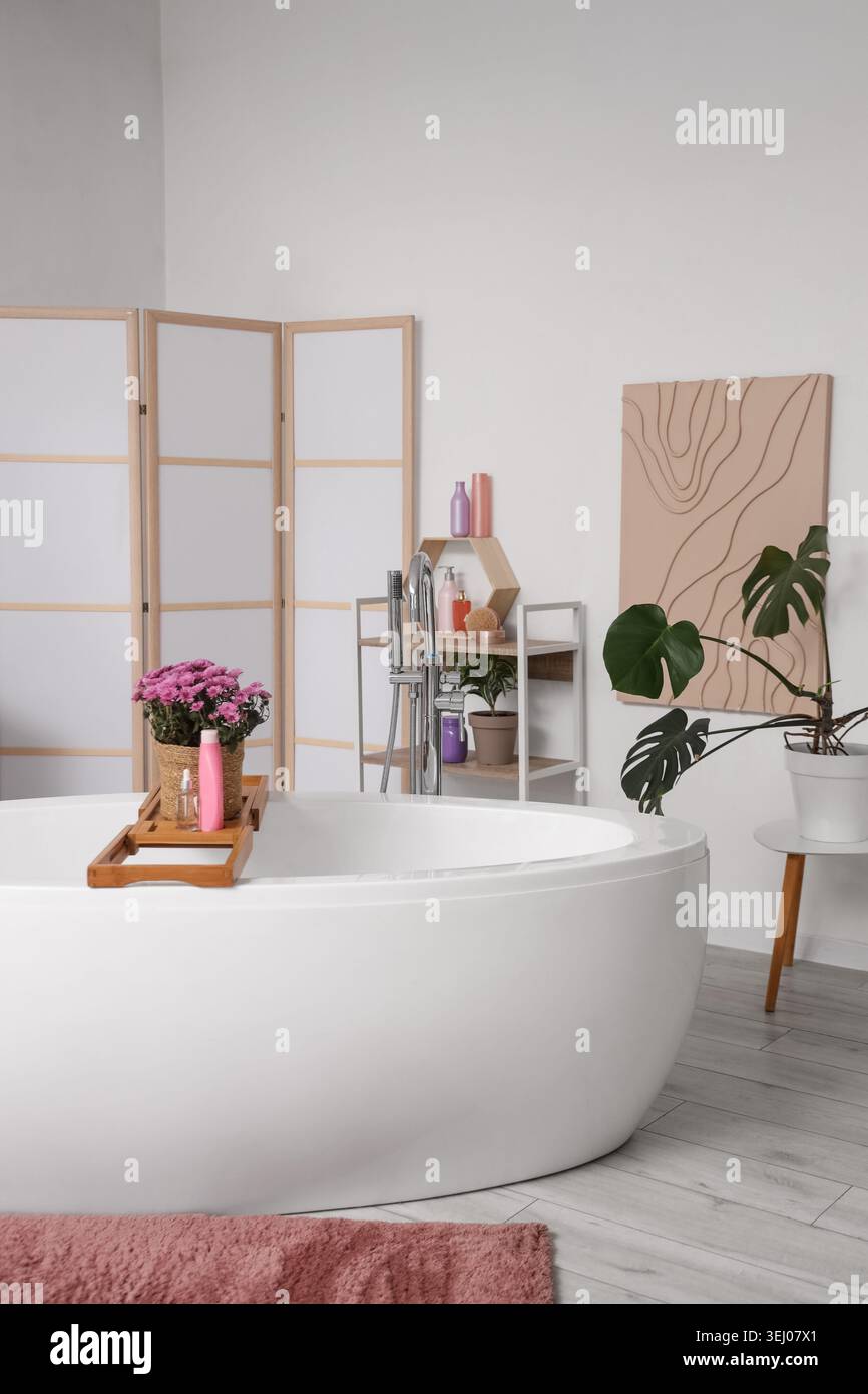 Interior of stylish bathroom with bathtub, folding screen and pink ...
