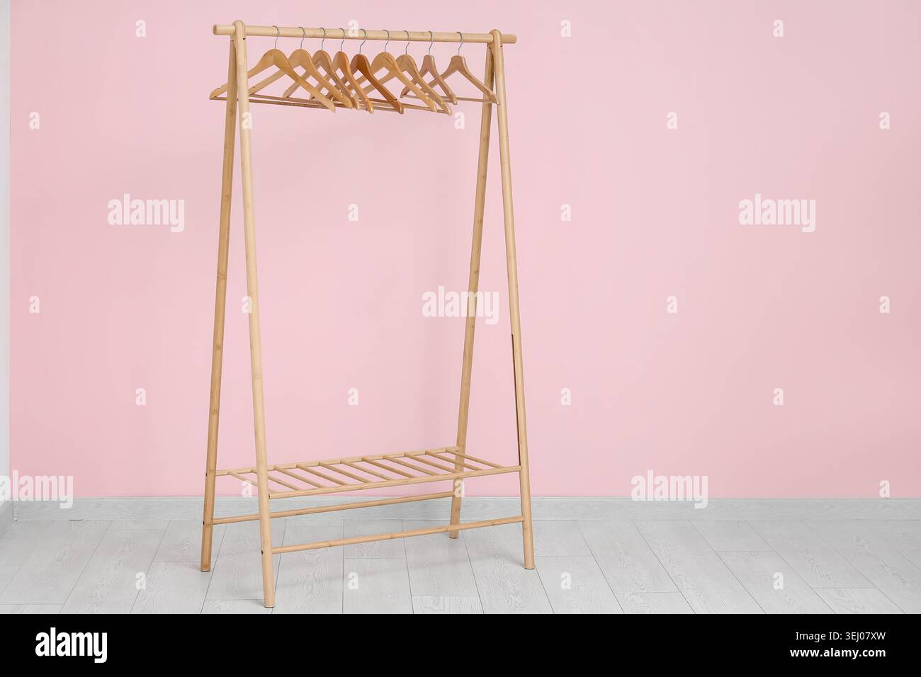 Wooden rack with hangers near pink wall Stock Photo - Alamy