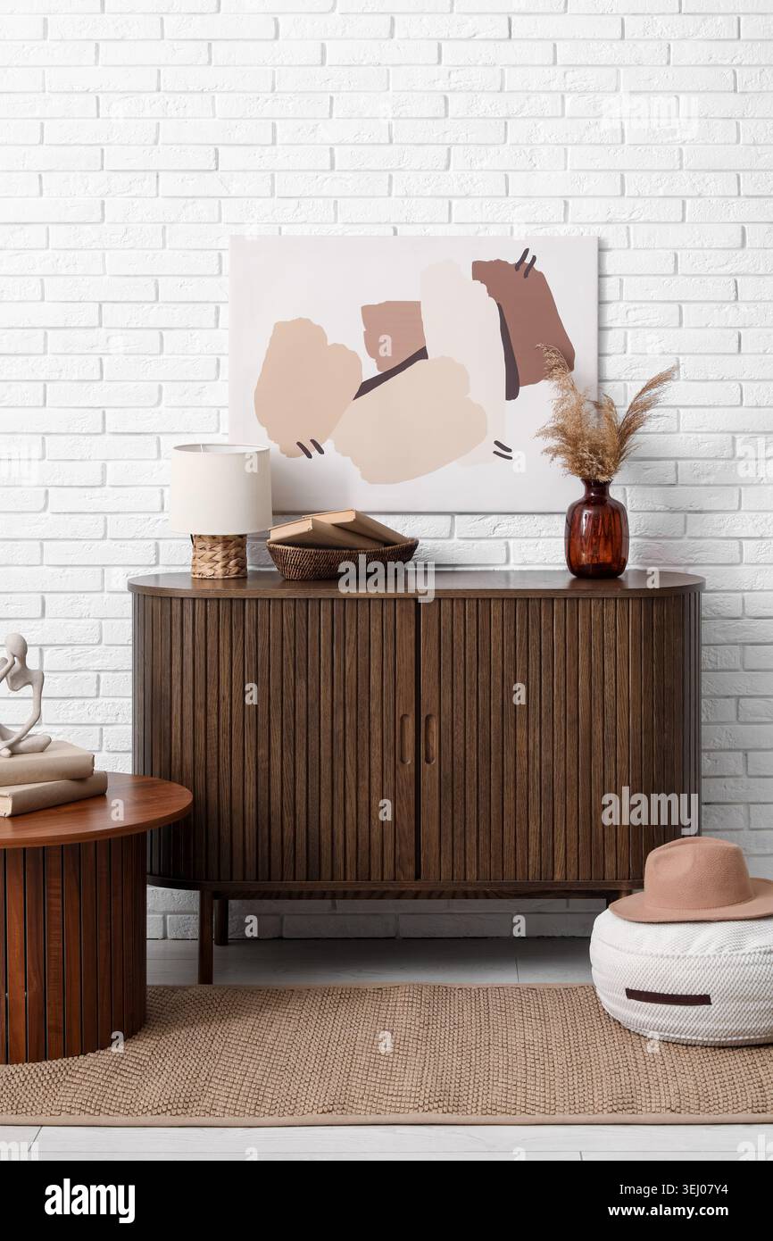 Chest of drawers with decor, coffee table and pouf near white brick ...