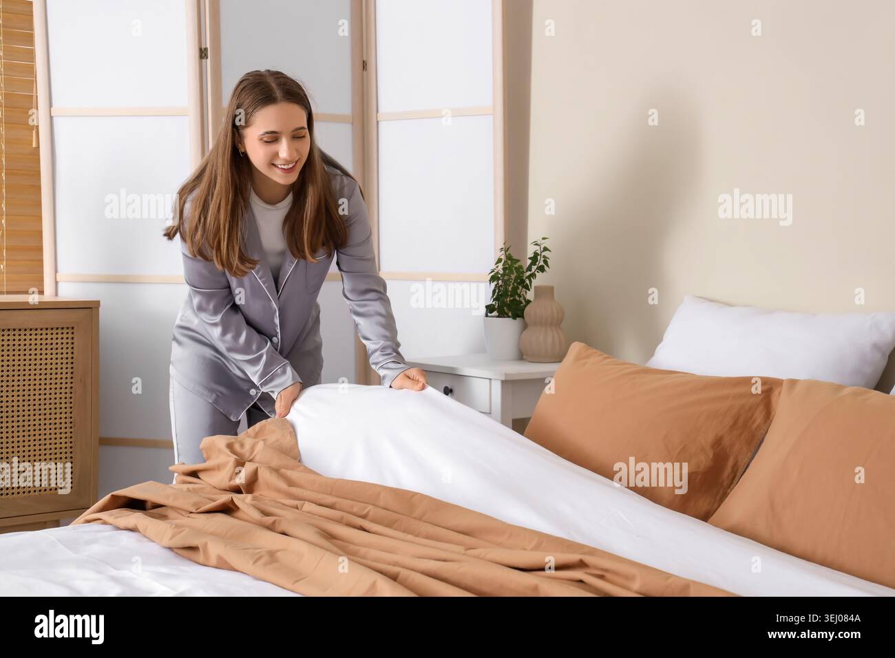 Pretty young woman making bed in stylish bedroom Stock Photo - Alamy