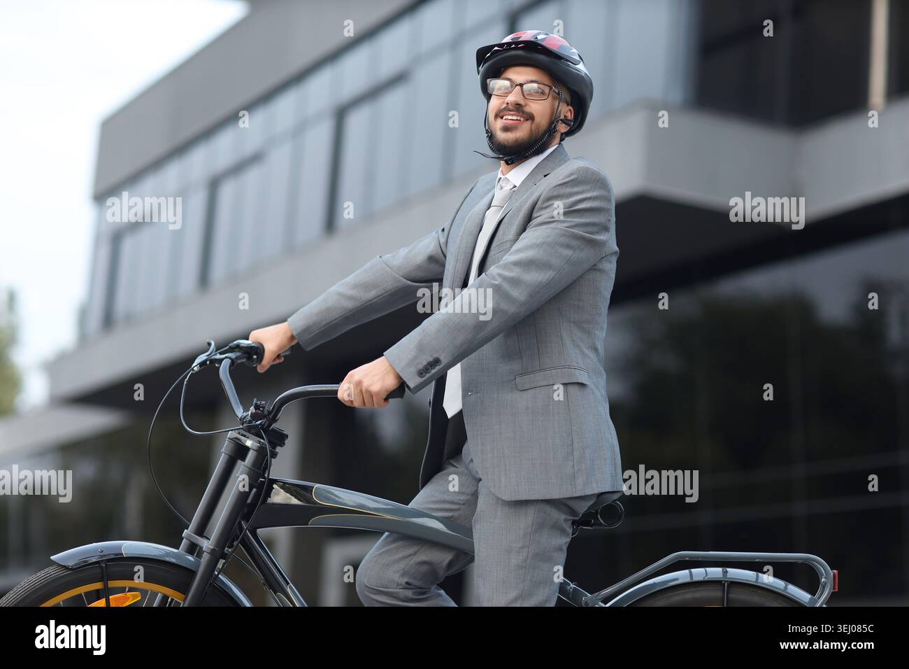 Young happy businessman in helmet with bicycle near office building on ...