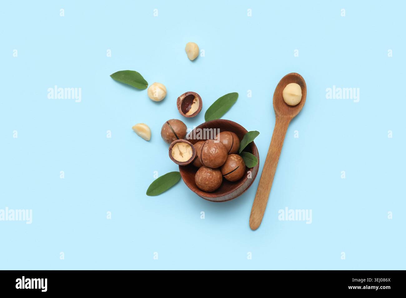 Wooden bowl and spoon with tasty macadamia nuts on blue background ...