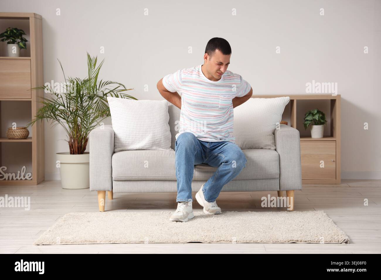 Young man suffering from back pain on sofa at home Stock Photo - Alamy