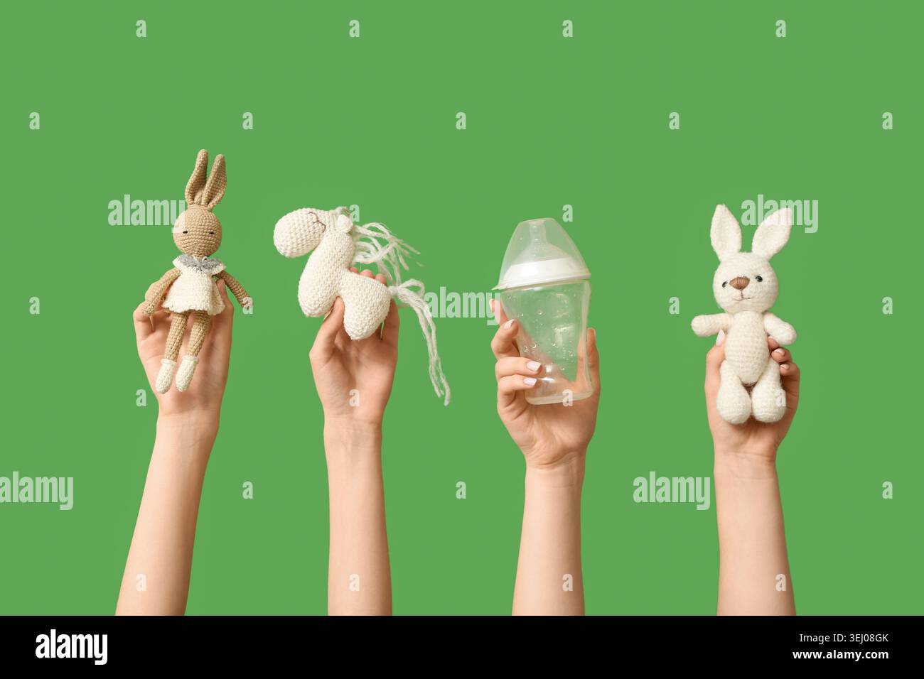 Female hands with baby bottle and knitted toys on green background ...