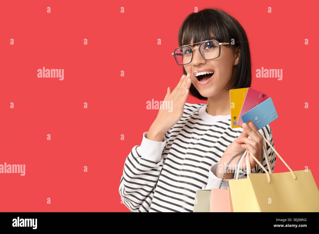Surprised young woman with credit cards and shopping bags on red ...