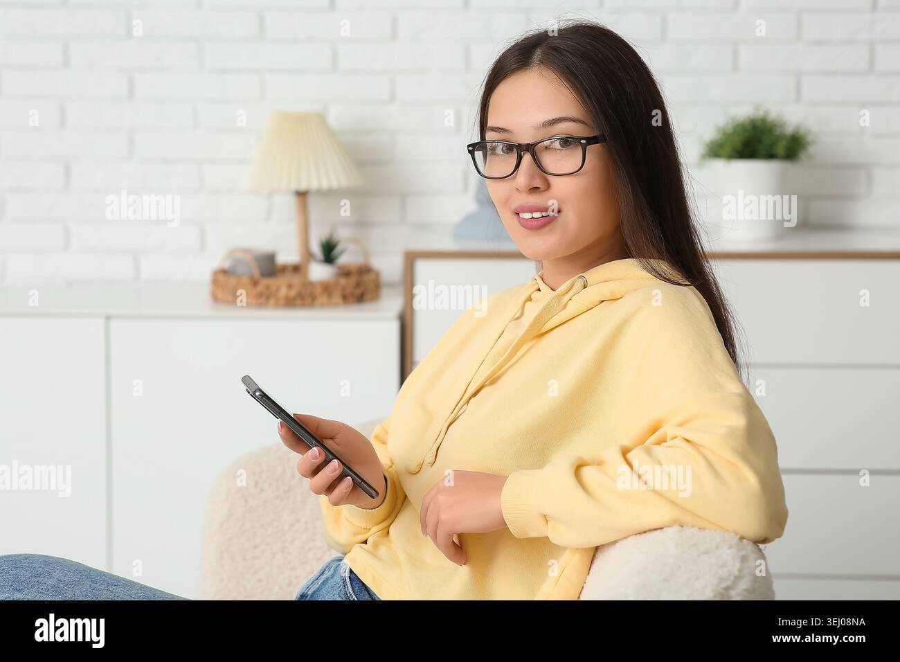 Young happy Asian woman in stylish eyeglasses with mobile phone sitting ...