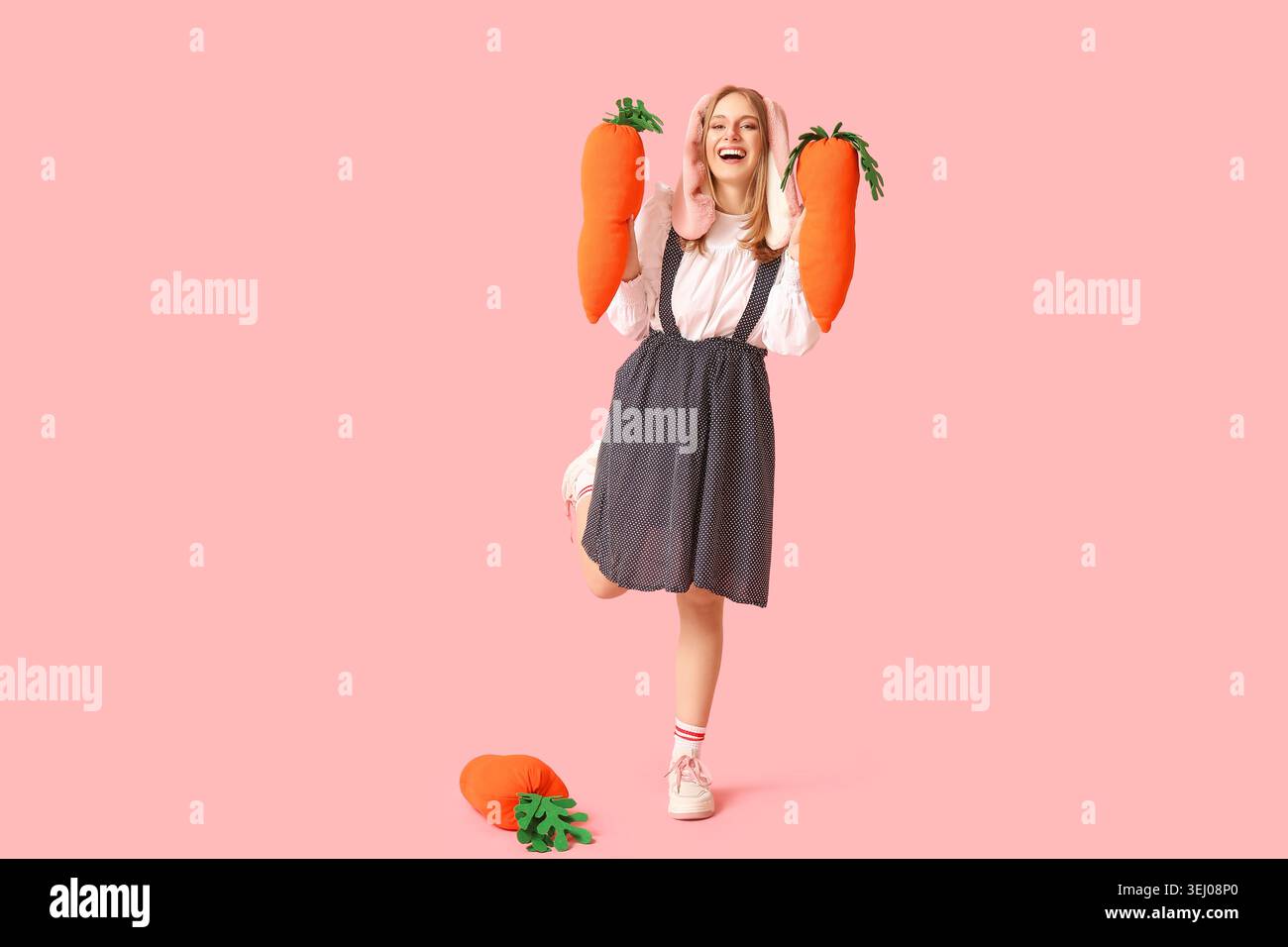 Happy woman in bunny ears with toy carrots on pink background. Easter ...