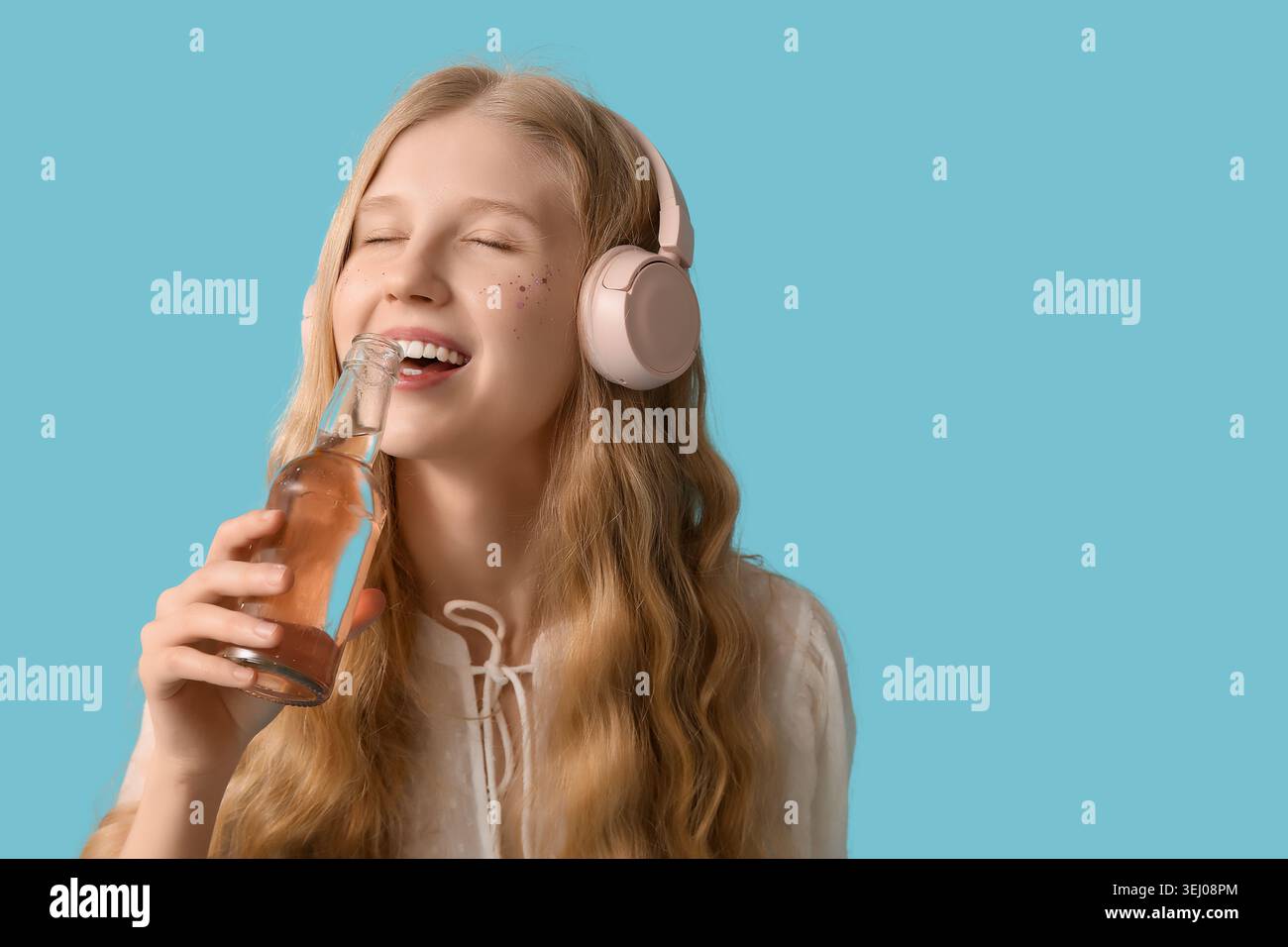 Beautiful young woman in headphones with bottle of soda on blue ...