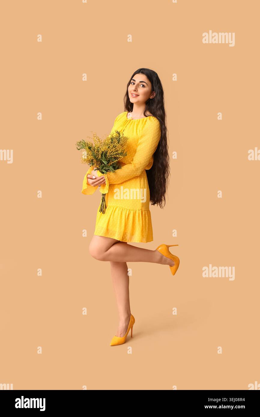 Beautiful young woman with bouquet of mimosa flowers on beige ...