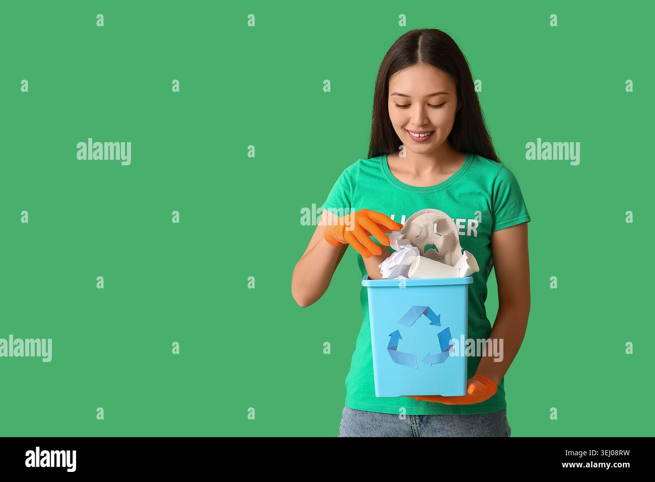 Young female volunteer holding recycle bin with garbage on green ...