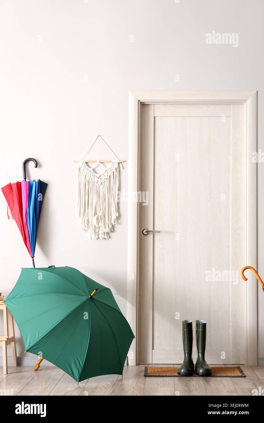 Interior of hallway with rubber boots and umbrellas near light wall ...