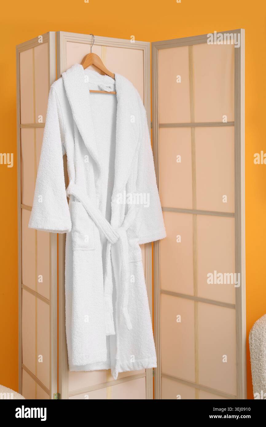 White bathrobe hanging on folding screen against yellow background ...