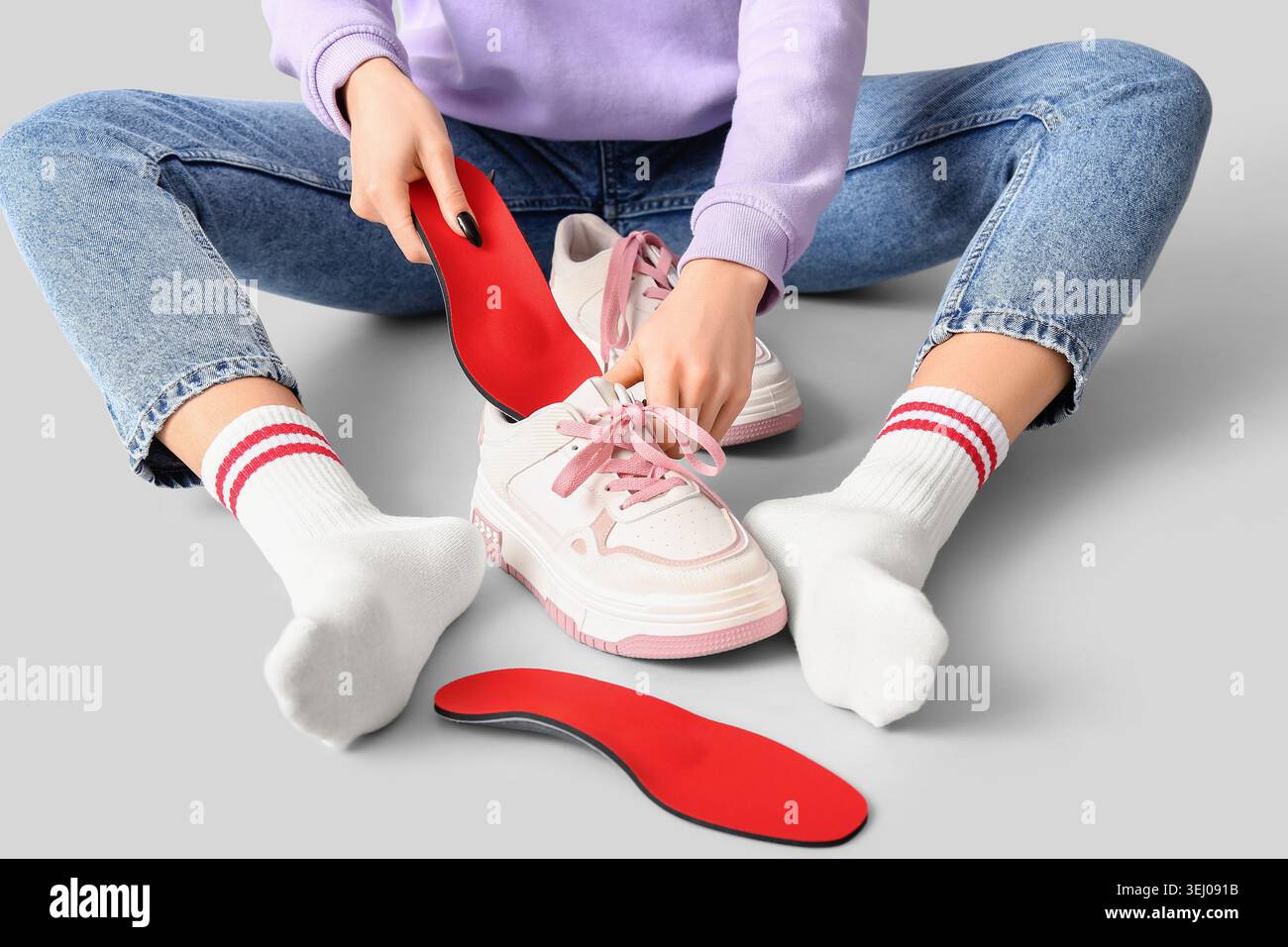 Young woman sitting and putting orthopedic insoles in sneakers isolated ...