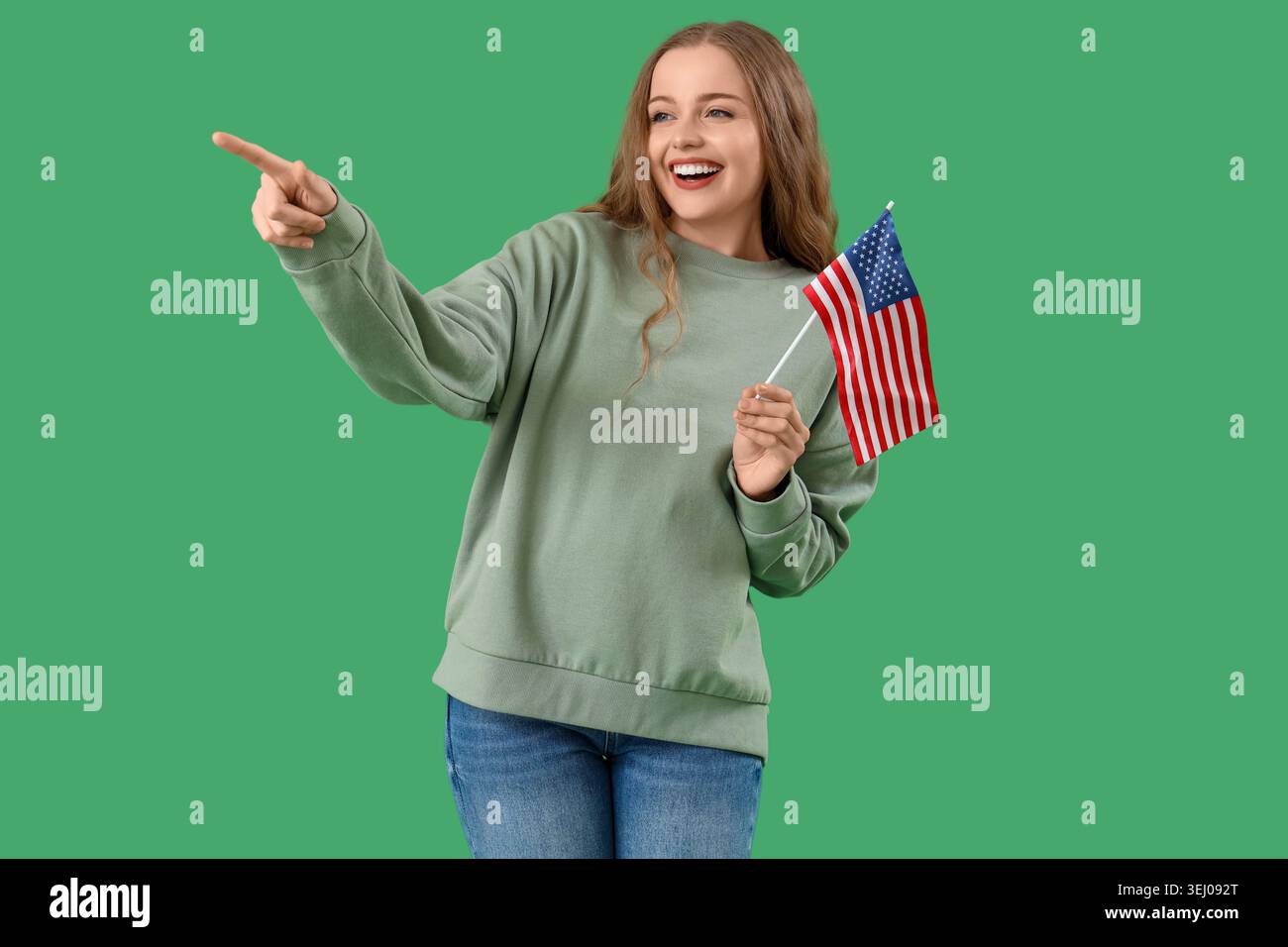 Laughing young woman with USA flag pointing at something on green ...