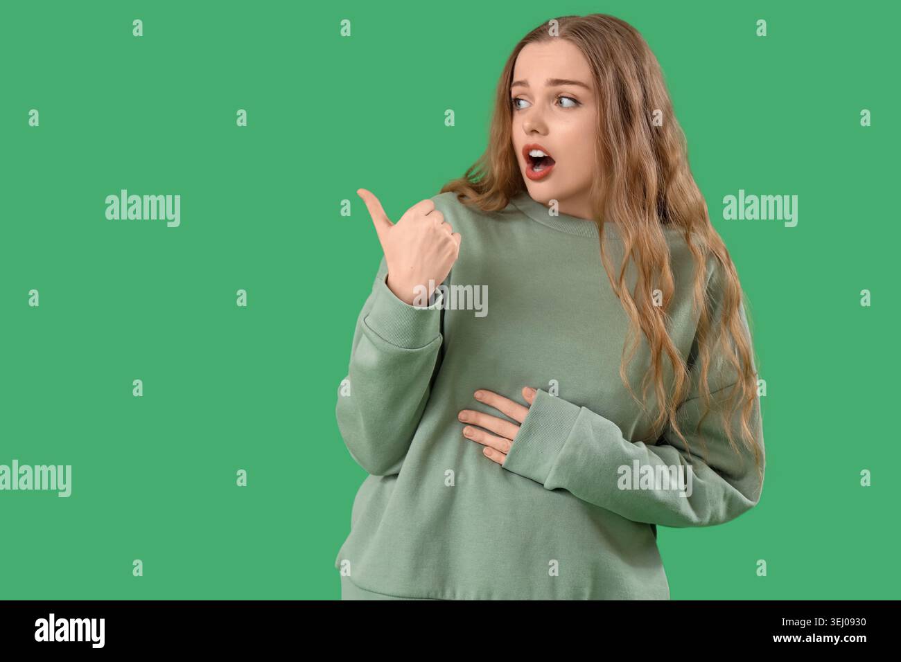 Shocked young woman pointing at something on green background ...