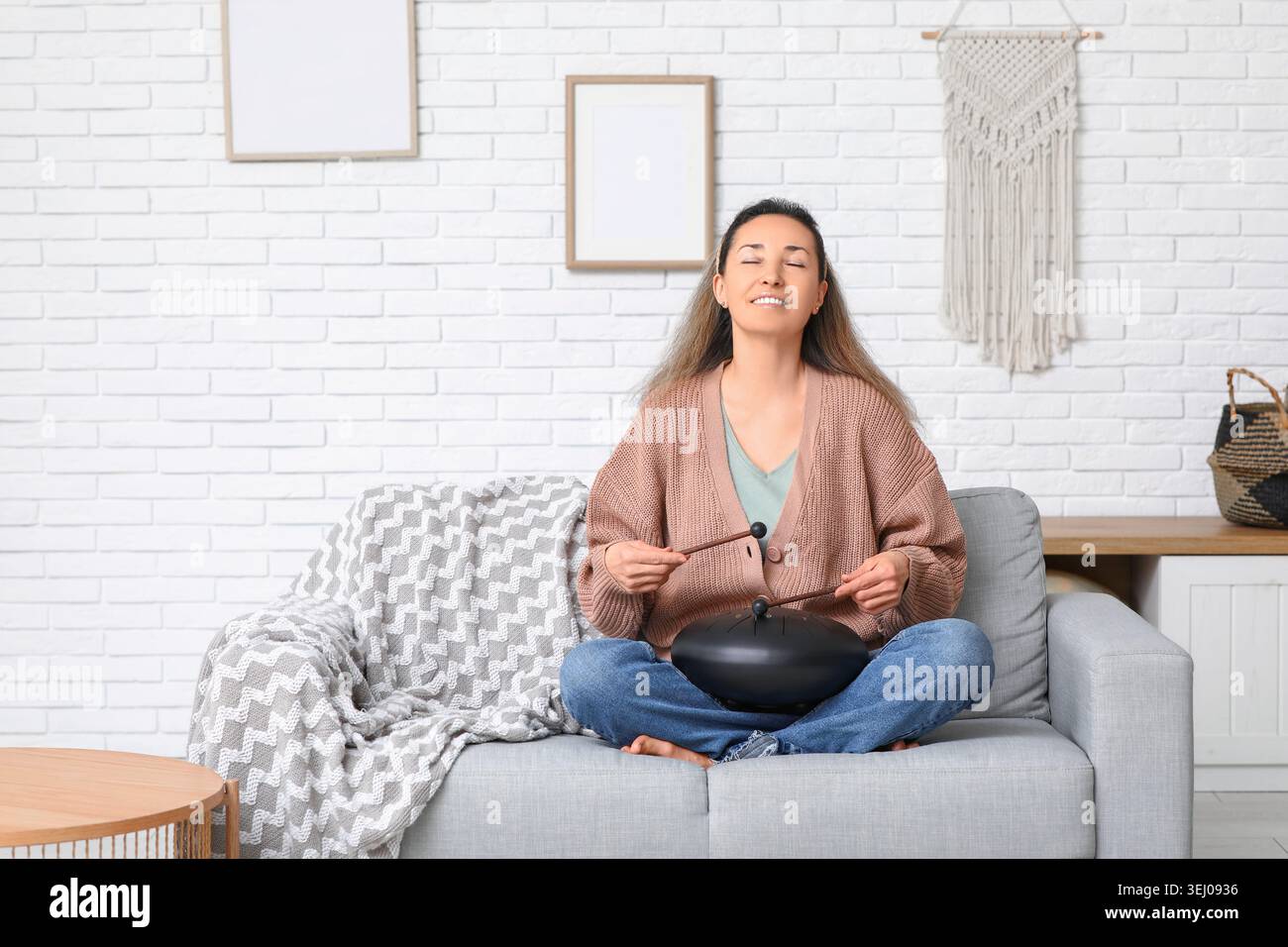 Beautiful mature woman with sticks playing glucophone on sofa at home ...