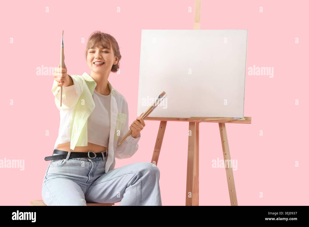 Female artist with paint brushes and easel on pink background Stock ...