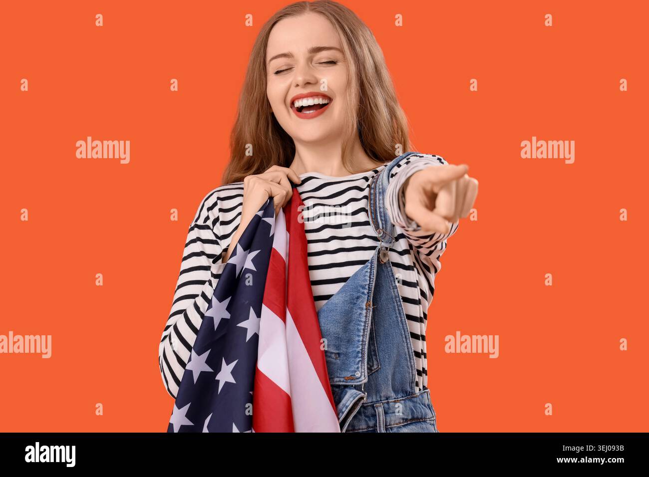 Laughing young woman with USA flag pointing at viewer on orange ...