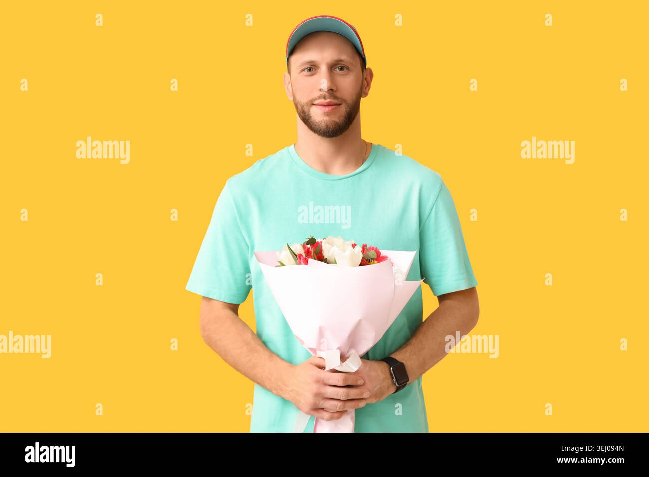 Young delivery man with bouquet of beautiful tulips on yellow ...