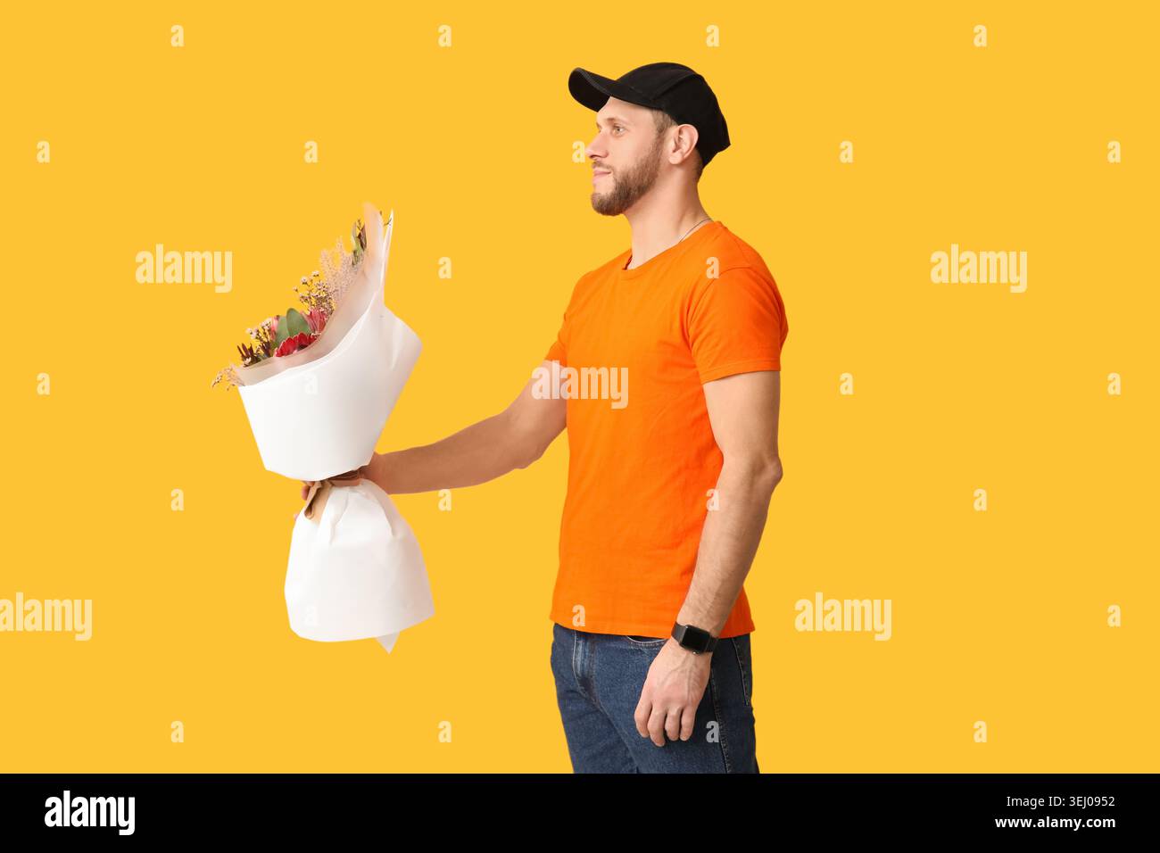 Young delivery man with bouquet of beautiful flowers on yellow ...