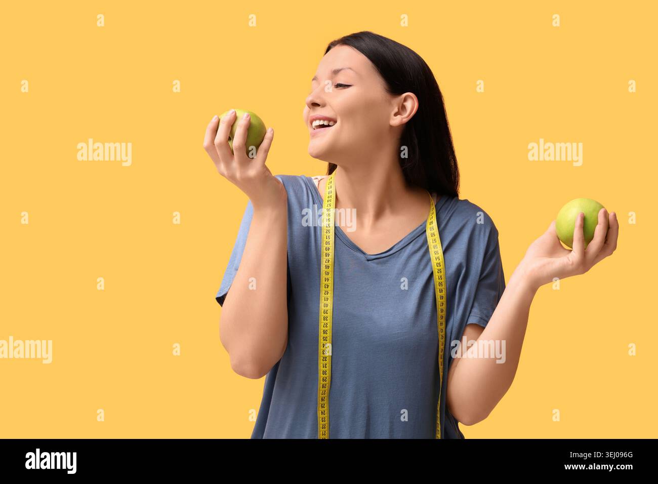 Beautiful young woman with measuring tape and fresh apples on yellow ...