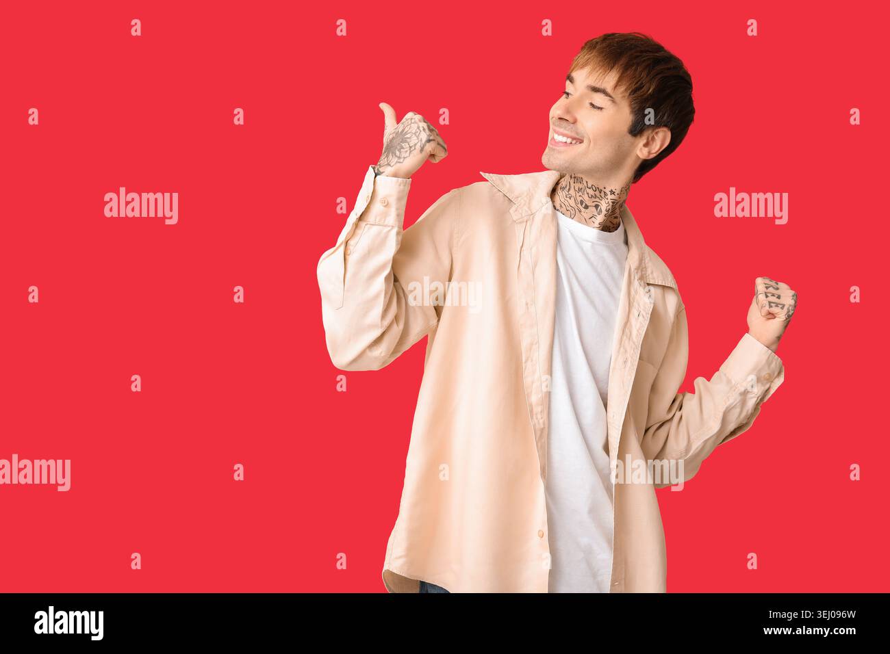 Happy handsome young tattooed man pointing at something on red ...
