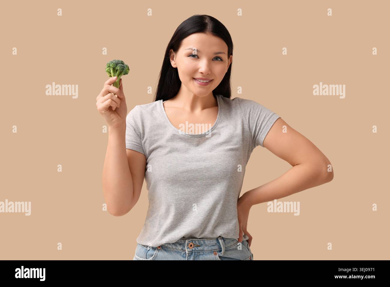 Beautiful young happy woman with fresh broccoli on beige background ...
