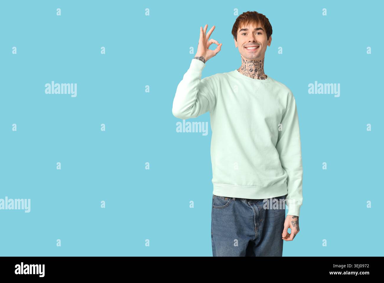 Happy handsome young tattooed man showing OK gesture on blue background ...