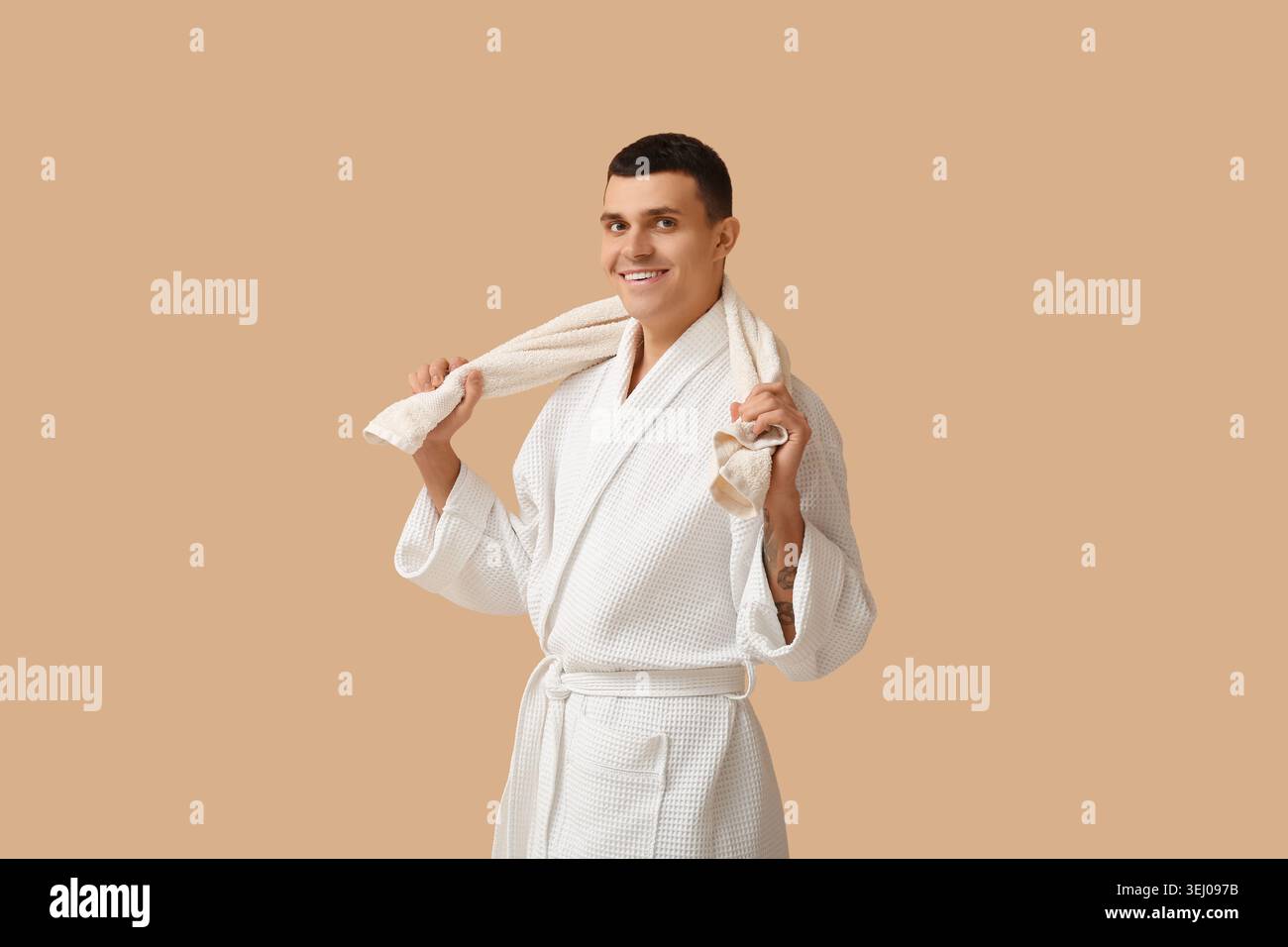 Portrait of handsome young man in bathrobe with towel on beige ...