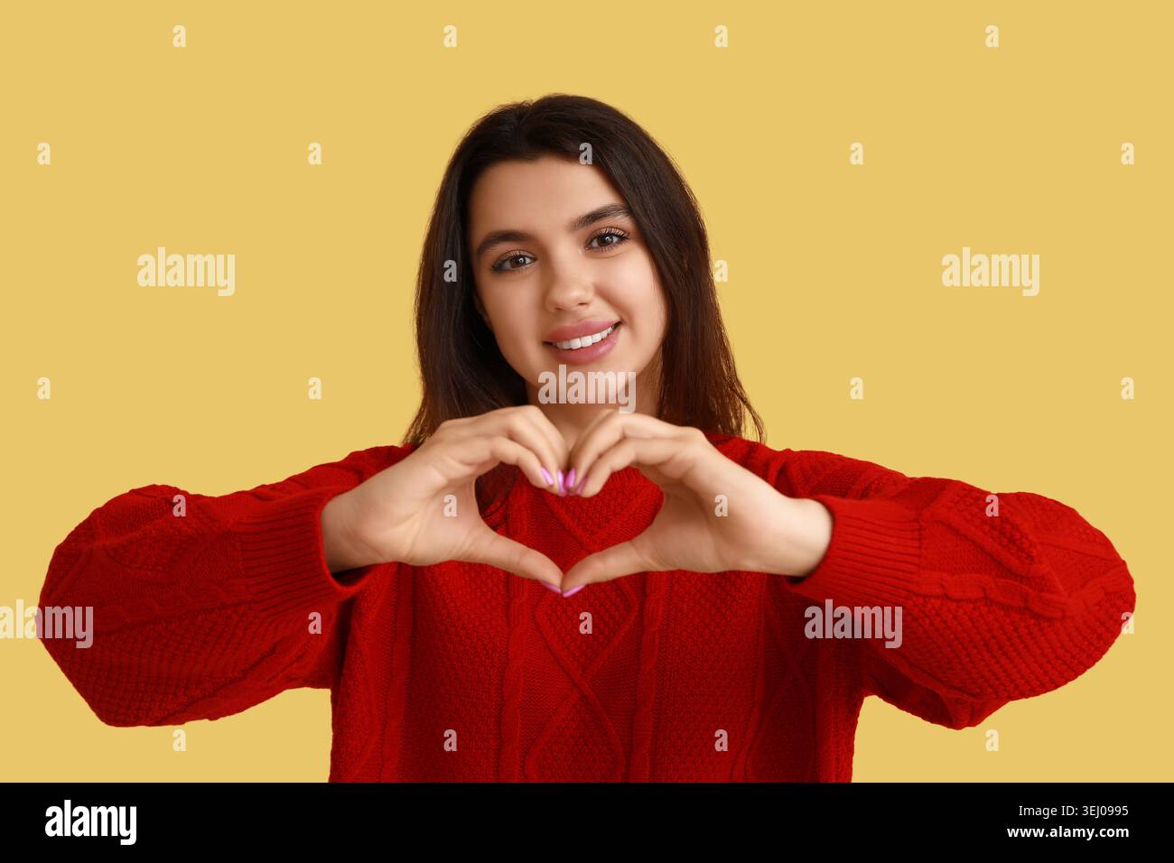 Happy young girl showing heart gesture on yellow background. Valentine ...