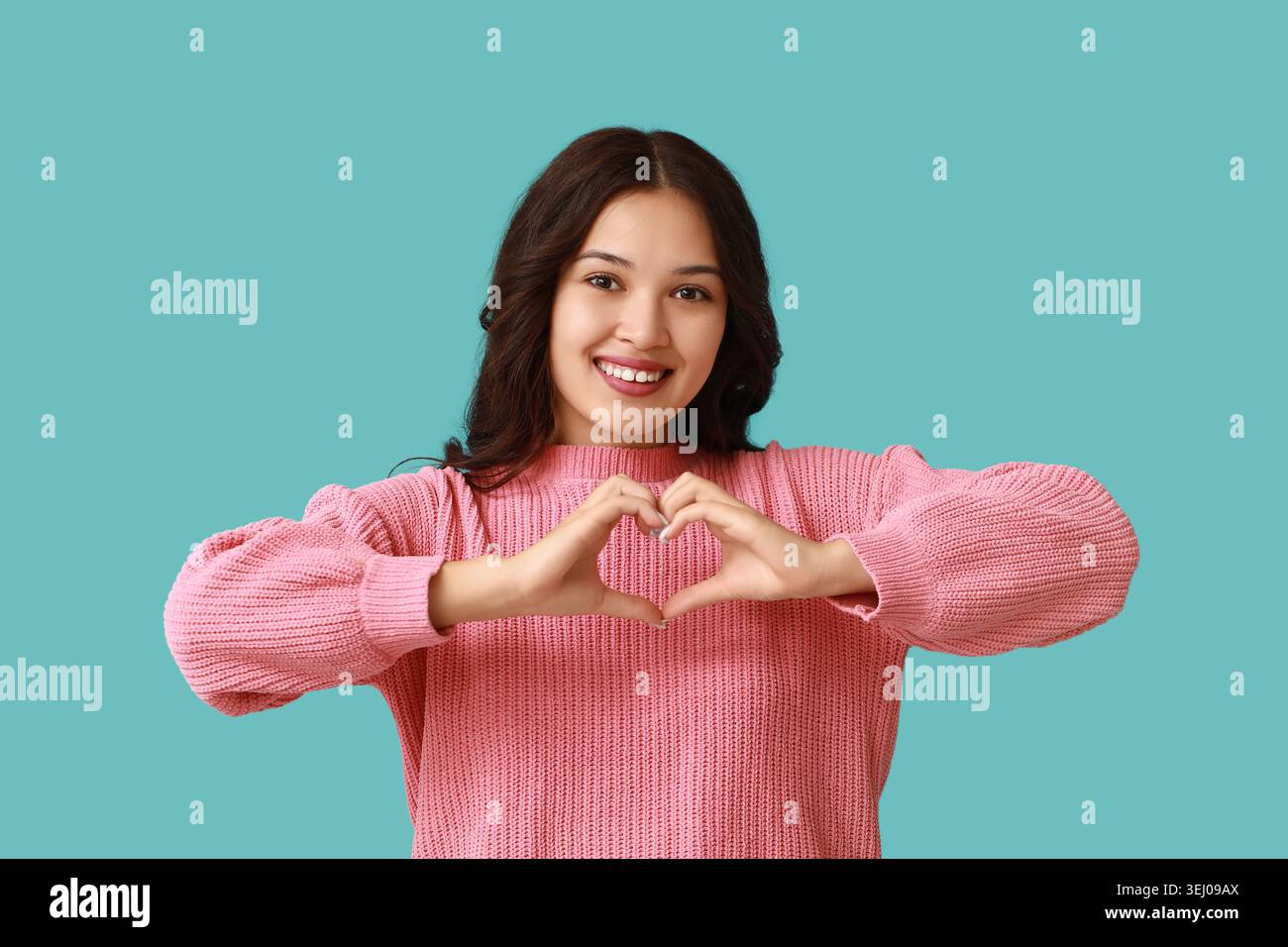 Happy young Asian woman showing heart gesture on blue background ...